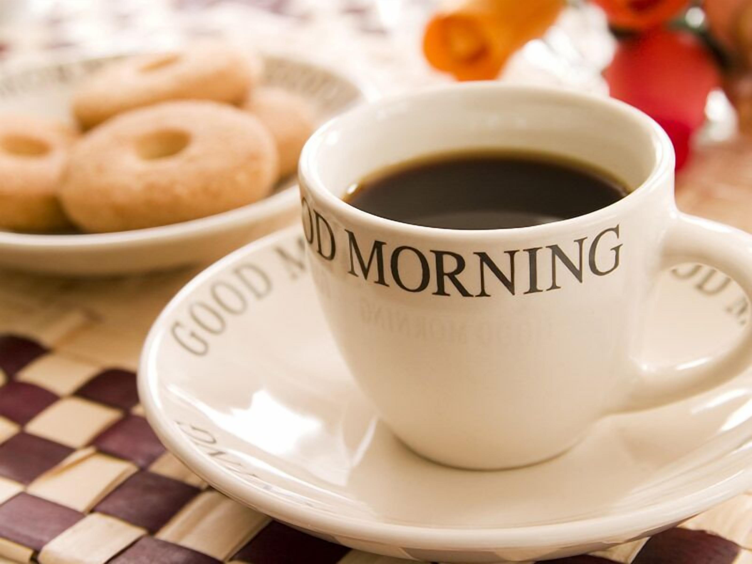 Uma xícara branca com a inscrição 'GOOD MORNING', apoiada em um pires.