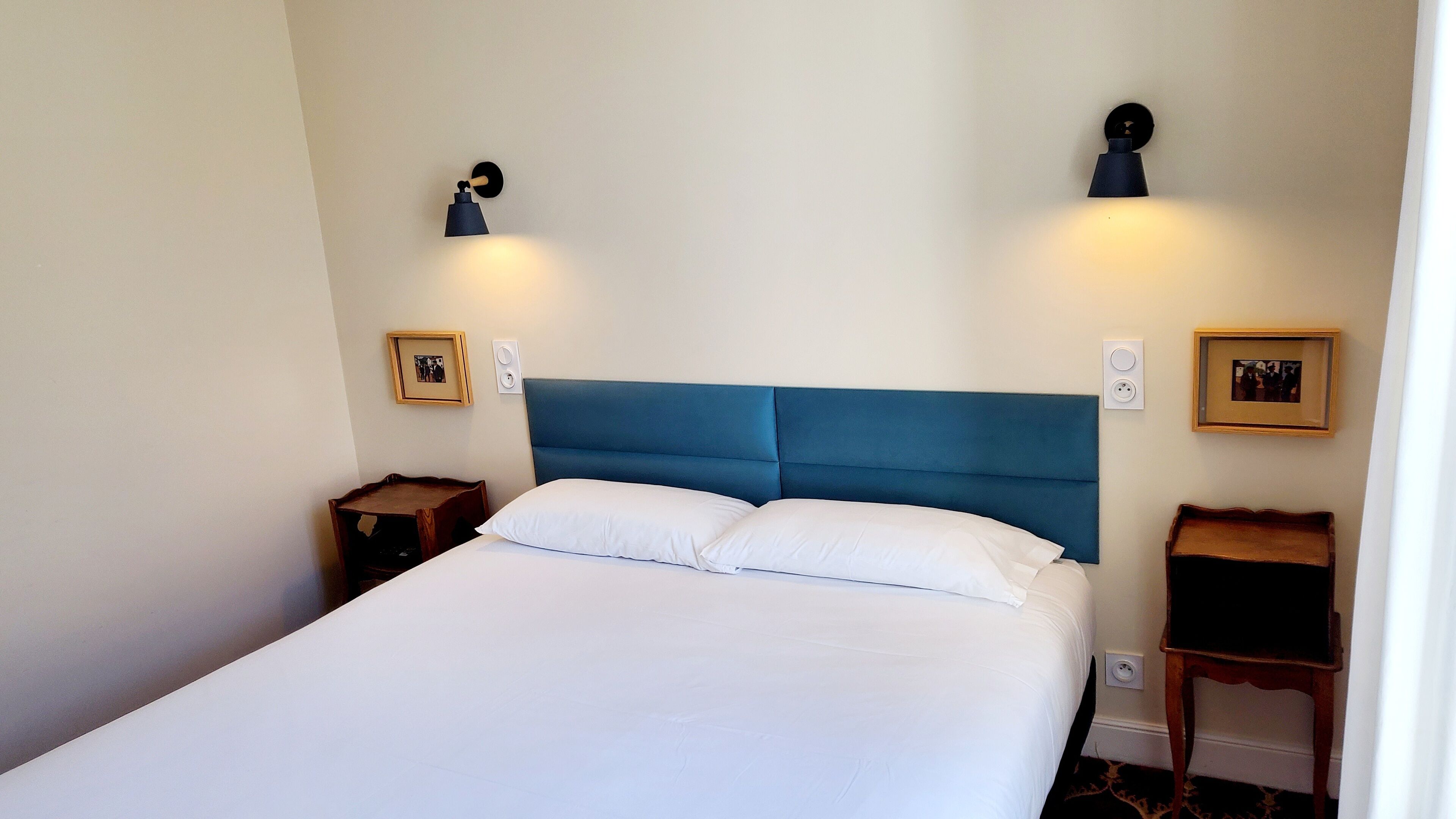 Quarto de hotel com uma cama grande, duas mesas de cabeceira, um criado-mudo e uma luminária na parede, além de um quadro emoldurado.