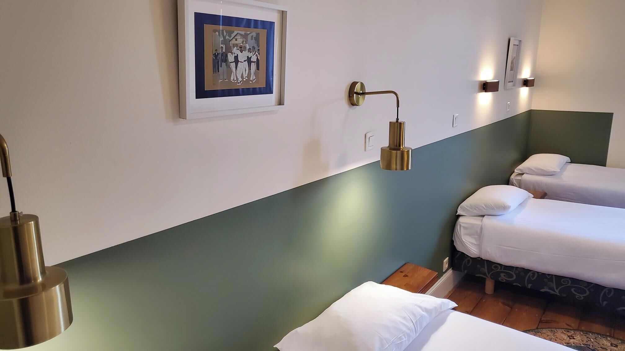 Quarto de hotel com duas camas, um quadro na parede e luminária fixada na parede.