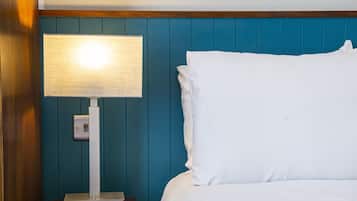Cama bem arrumada com lençóis e travesseiro brancos, mesa de cabeceira branca com abajur e painéis de parede em tom de verde-água.