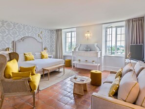 Quarto de hotel com cama, sofá, televisão e vista para o exterior.