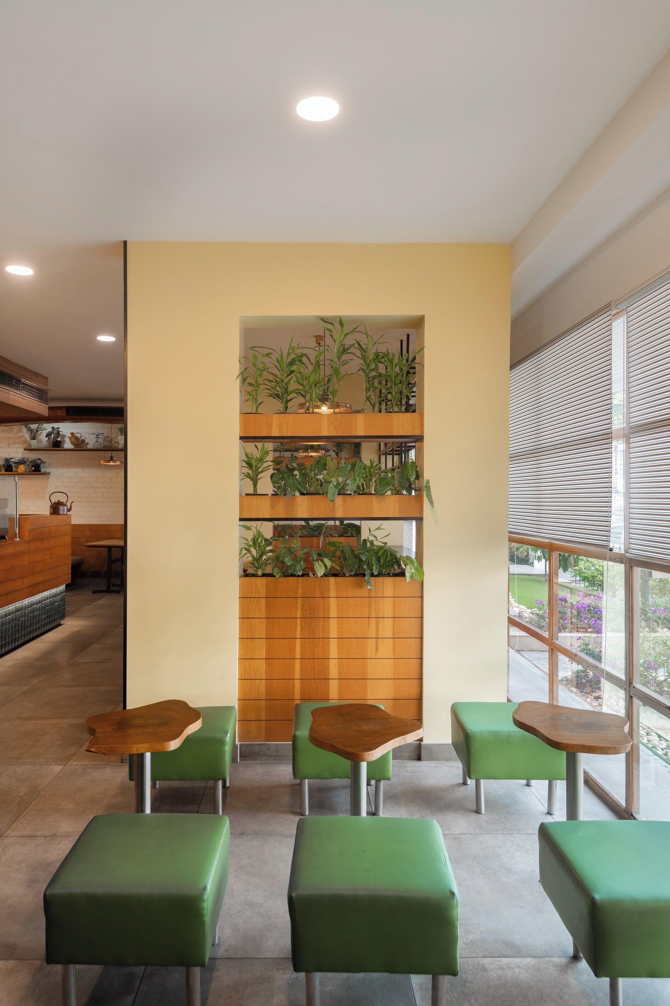 Decoração moderna com assentos verdes, mesas de madeira e uma parede vertical com plantas.