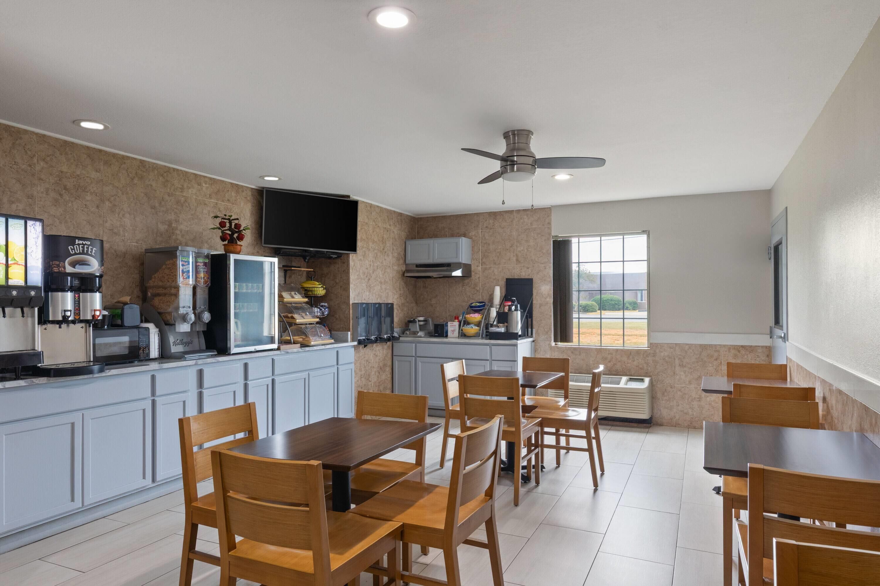 Cozinha moderna com armários cinza, espaço para café e área de refeições com mesas e cadeiras de madeira.