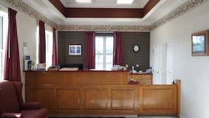 Uma área de recepção com uma mesa de madeira, um relógio na parede e uma placa emoldurada acima da mesa.