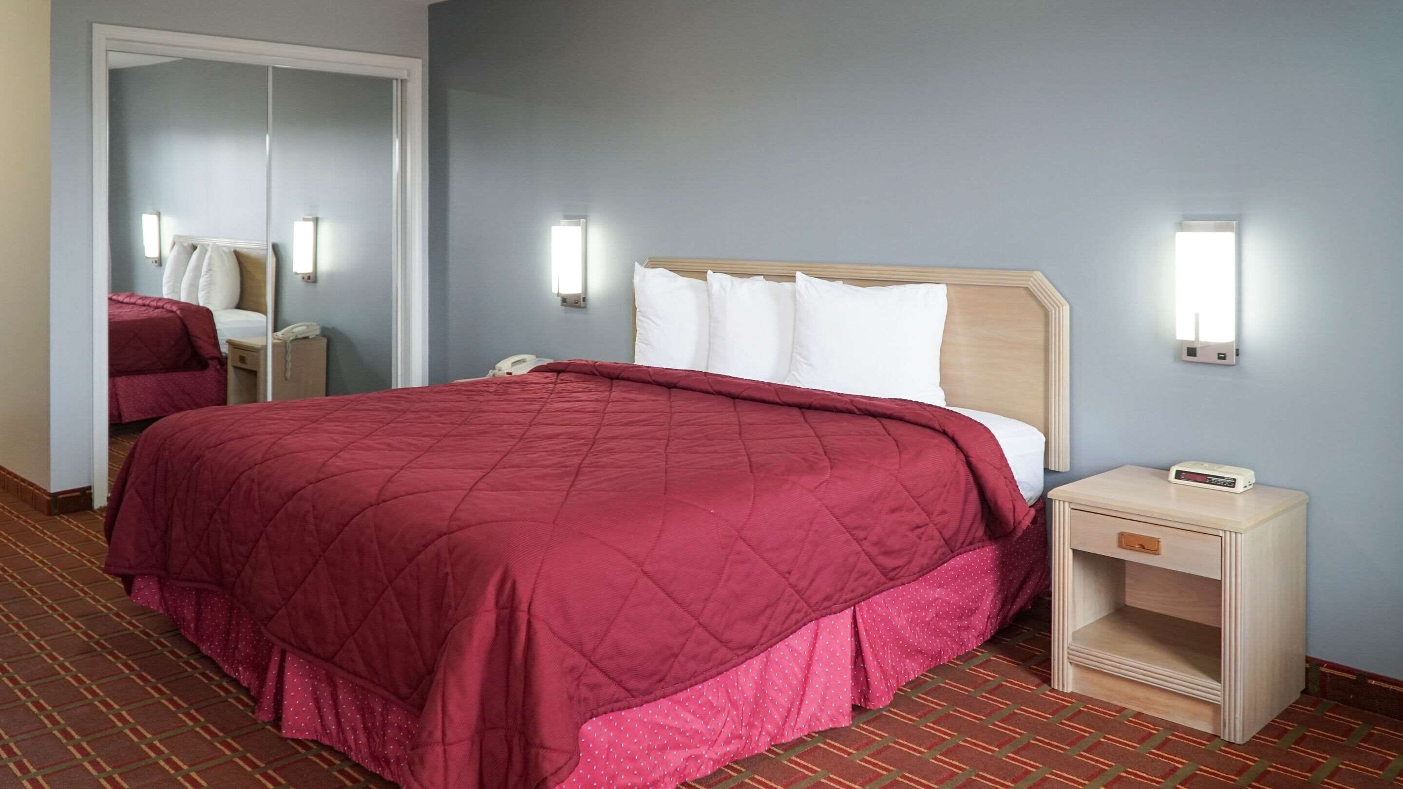 Quarto de hotel com uma cama grande, mesa de cabeceira com luminária, espelho e telefone.