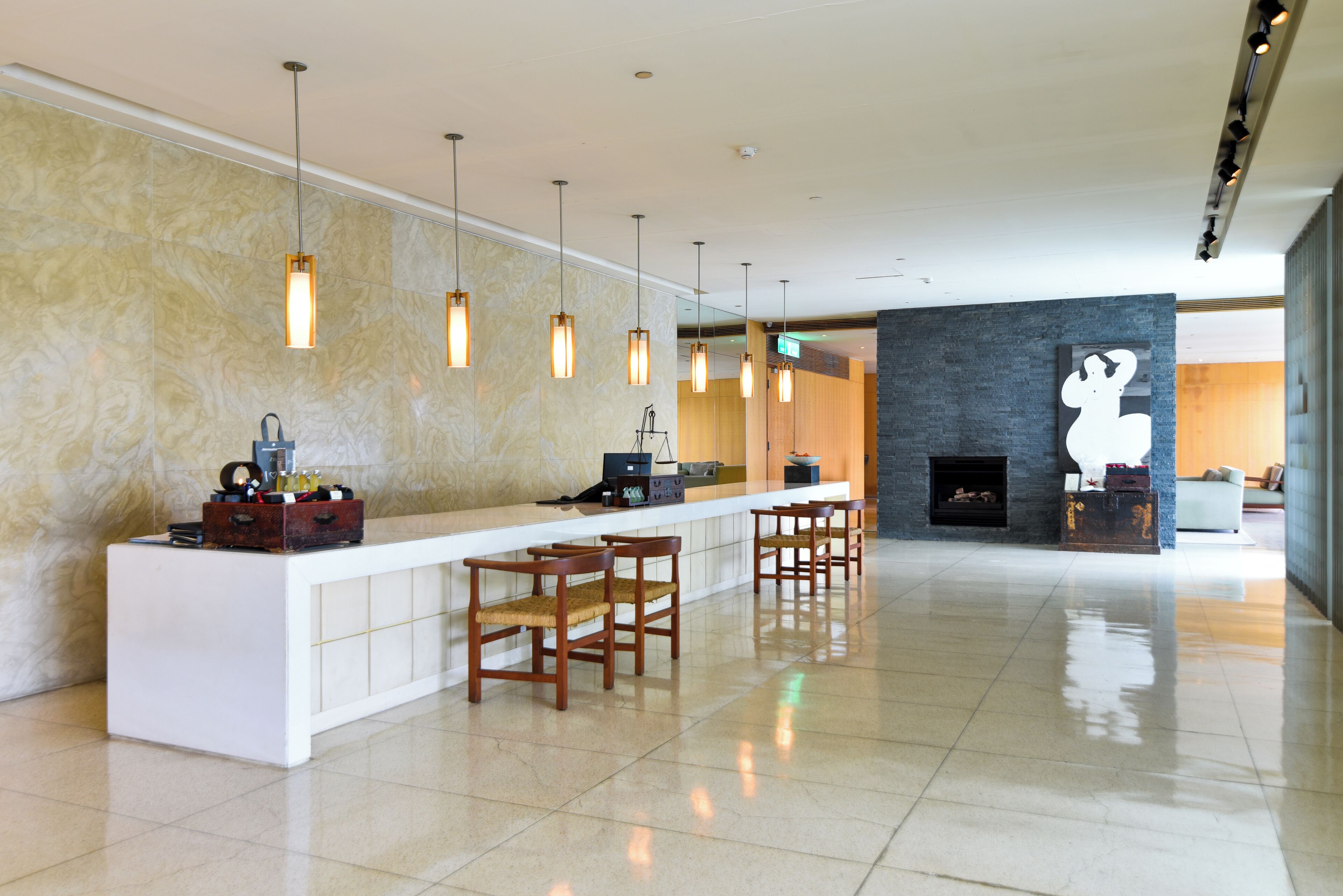 Um lobby moderno com balcão de recepção, cadeiras de madeira, luminárias pendentes, lareira e uma grande obra de arte abstrata na parede.