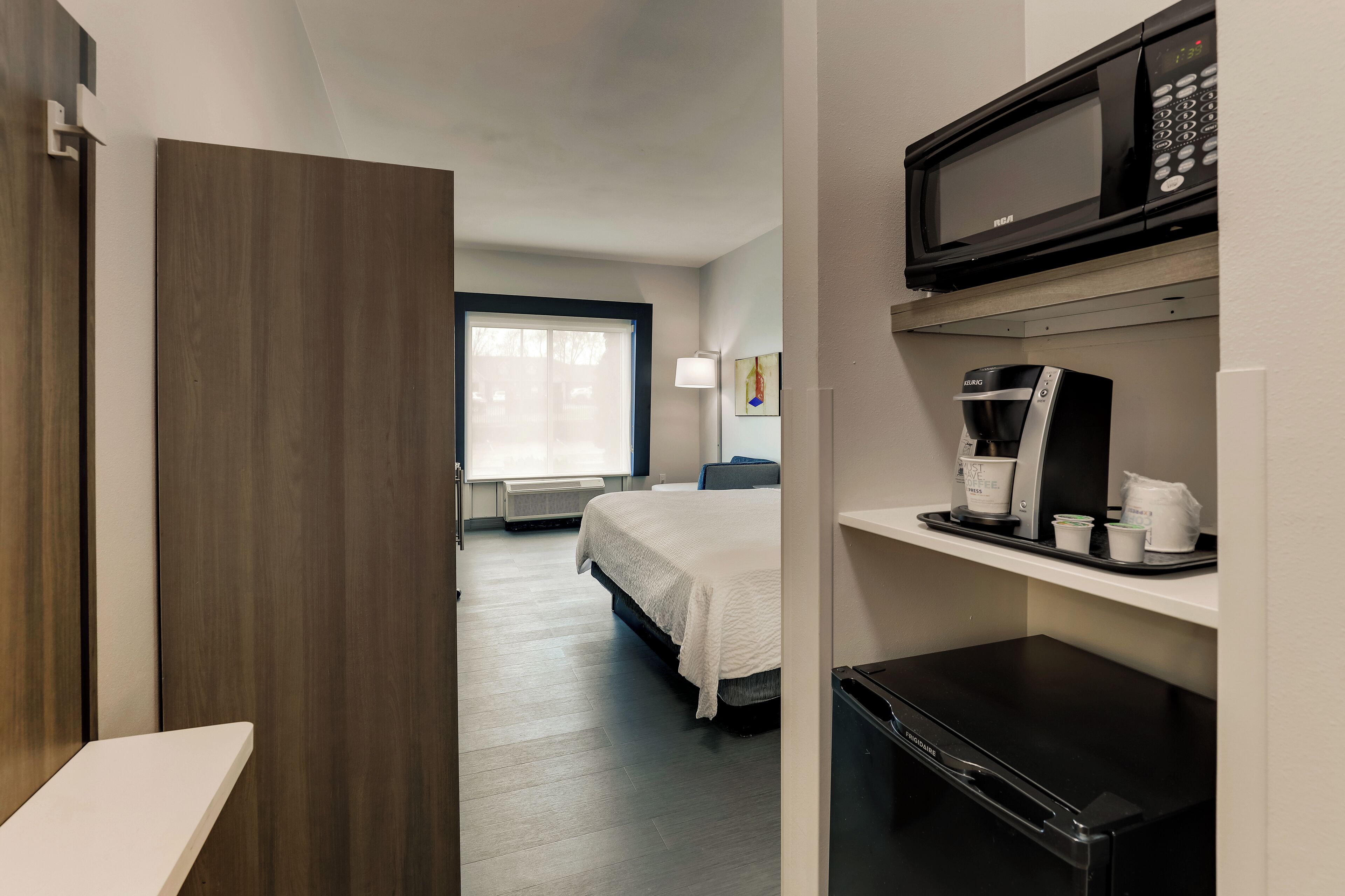 Quarto de hotel com cama, micro-ondas, cafeteira e lixeira.
