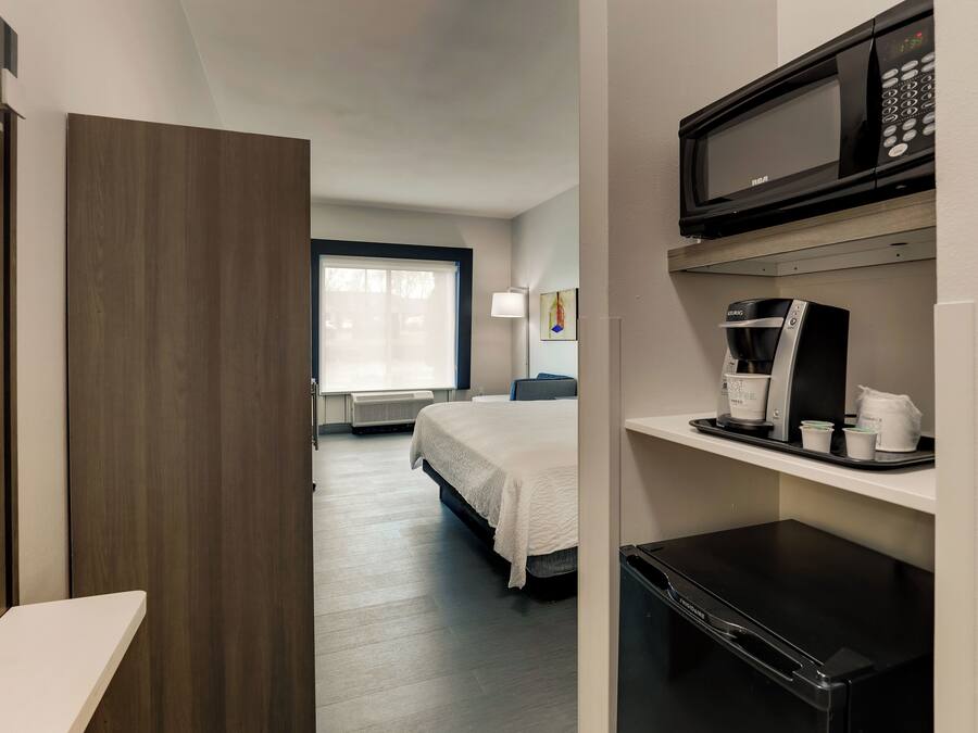 Quarto de hotel com cama, micro-ondas, cafeteira e lixeira.