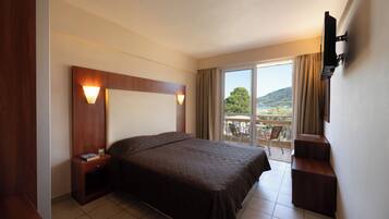 Quarto de hotel com uma cama grande, mesa de cabeceira, TV na parede e varanda com vista para o exterior.
