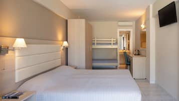 Quarto de hotel com uma cama grande, uma escrivaninha, uma beliche e um banheiro visível através de uma porta aberta.