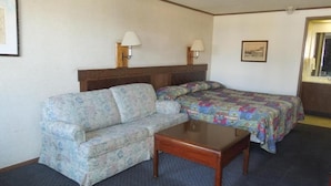 Quarto de hotel com uma cama, um sofá, uma mesinha e duas luminárias na parede.