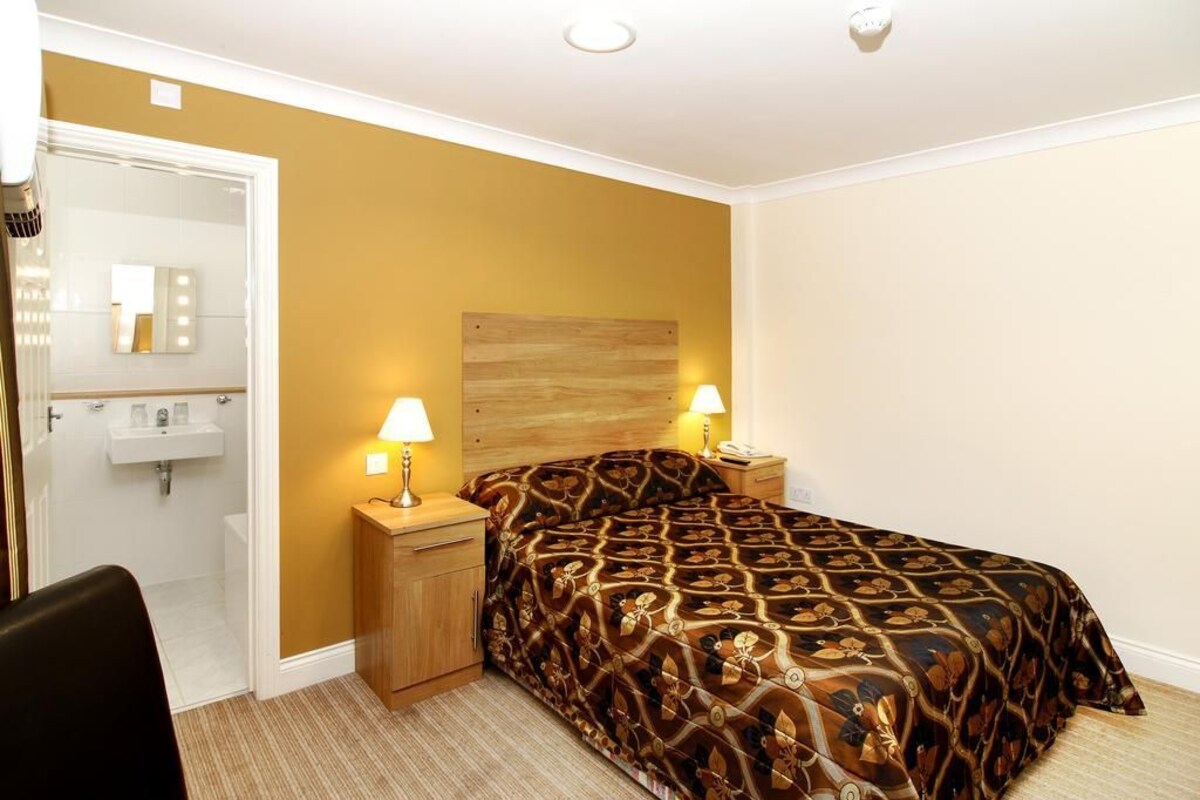 Quarto de hotel com cama, mesas de cabeceira, um espelho e banheiro com pia e espelho.