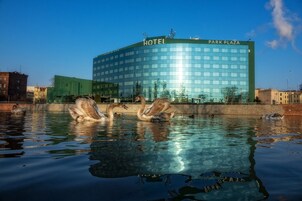 Hotel moderno com fachada de vidro, cisnes na água e céu azul límpido.