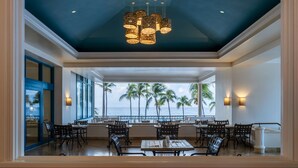Uma sala de jantar ampla com vista para o oceano, com um lustre moderno e mobiliário elegante.