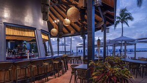 Uma área de bar ao ar livre com móveis de vime, balcão e guarda-sóis.