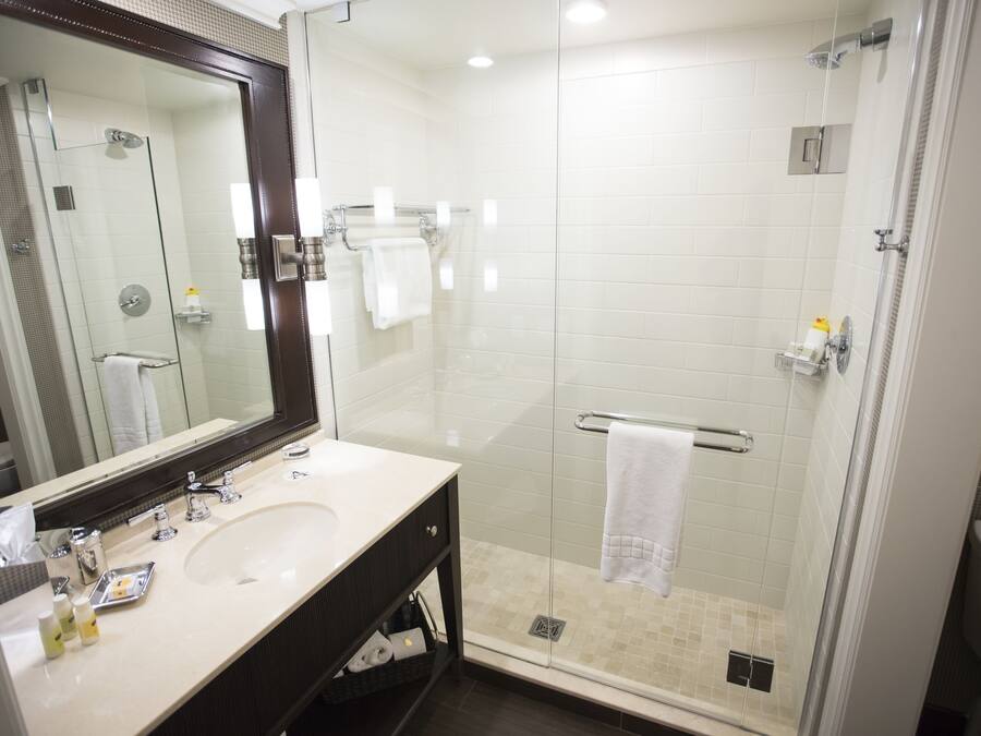 Uma casa de banho moderna com cabine de duche em vidro, um espelho grande e uma toucador com lavatório e artigos de higiene pessoal.