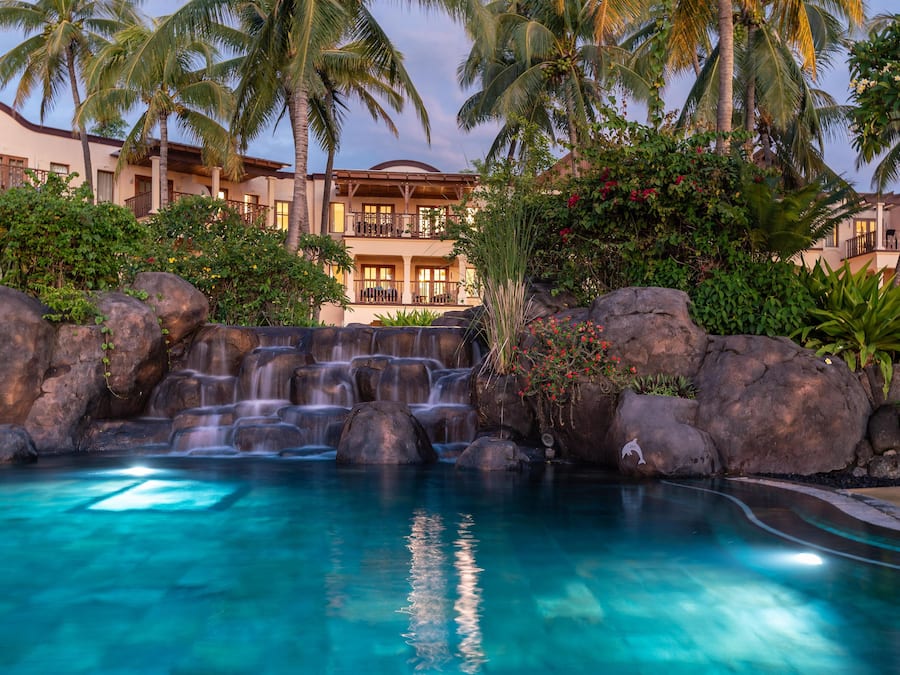 Um resort com piscina, palmeiras e uma cascata.