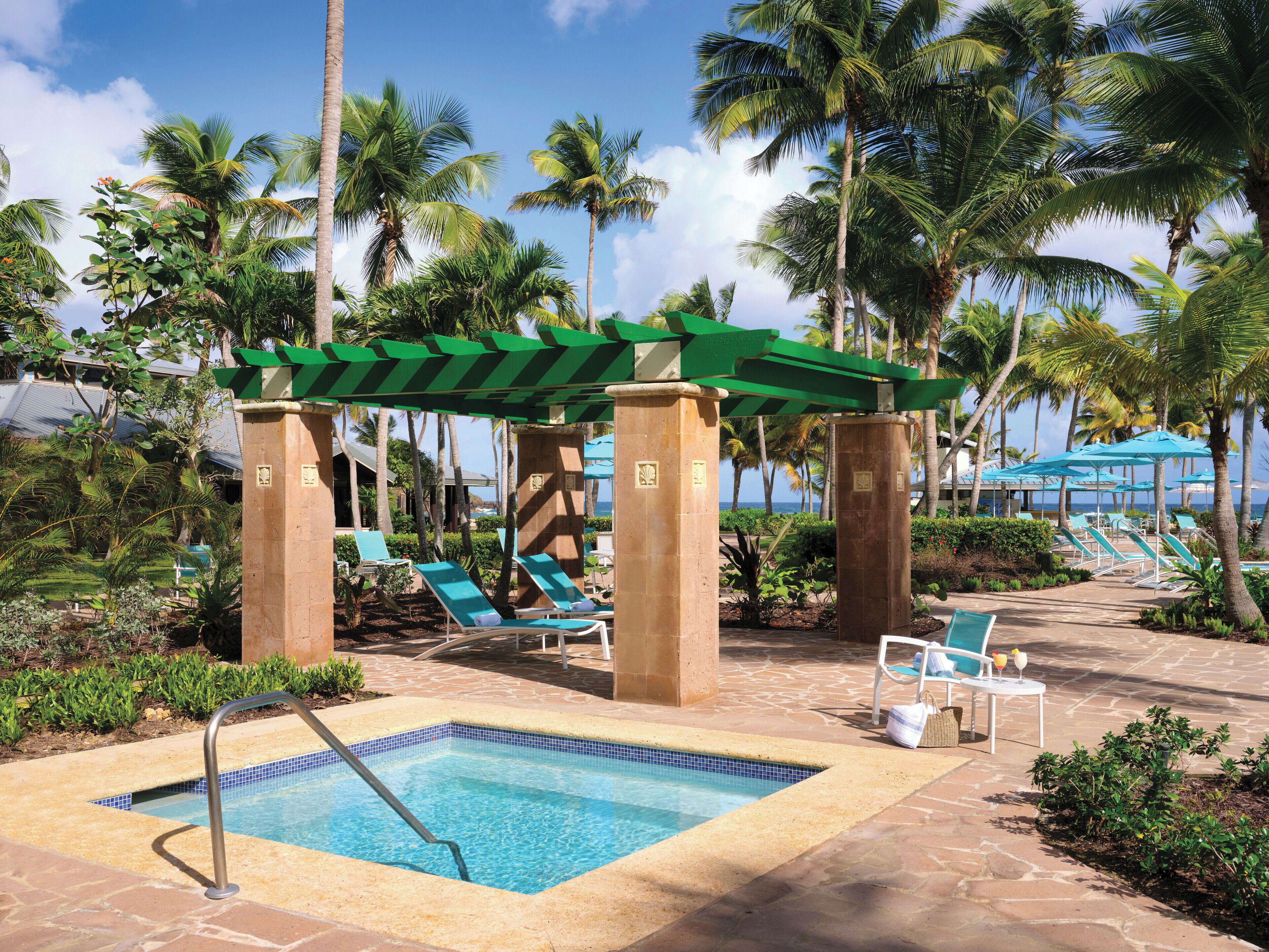 Uma área de piscina com piscina azulejada, espreguiçadeiras e um pérgola com telhado verde.