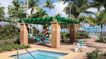 Uma área de piscina com piscina azulejada, espreguiçadeiras e um pérgola com telhado verde.