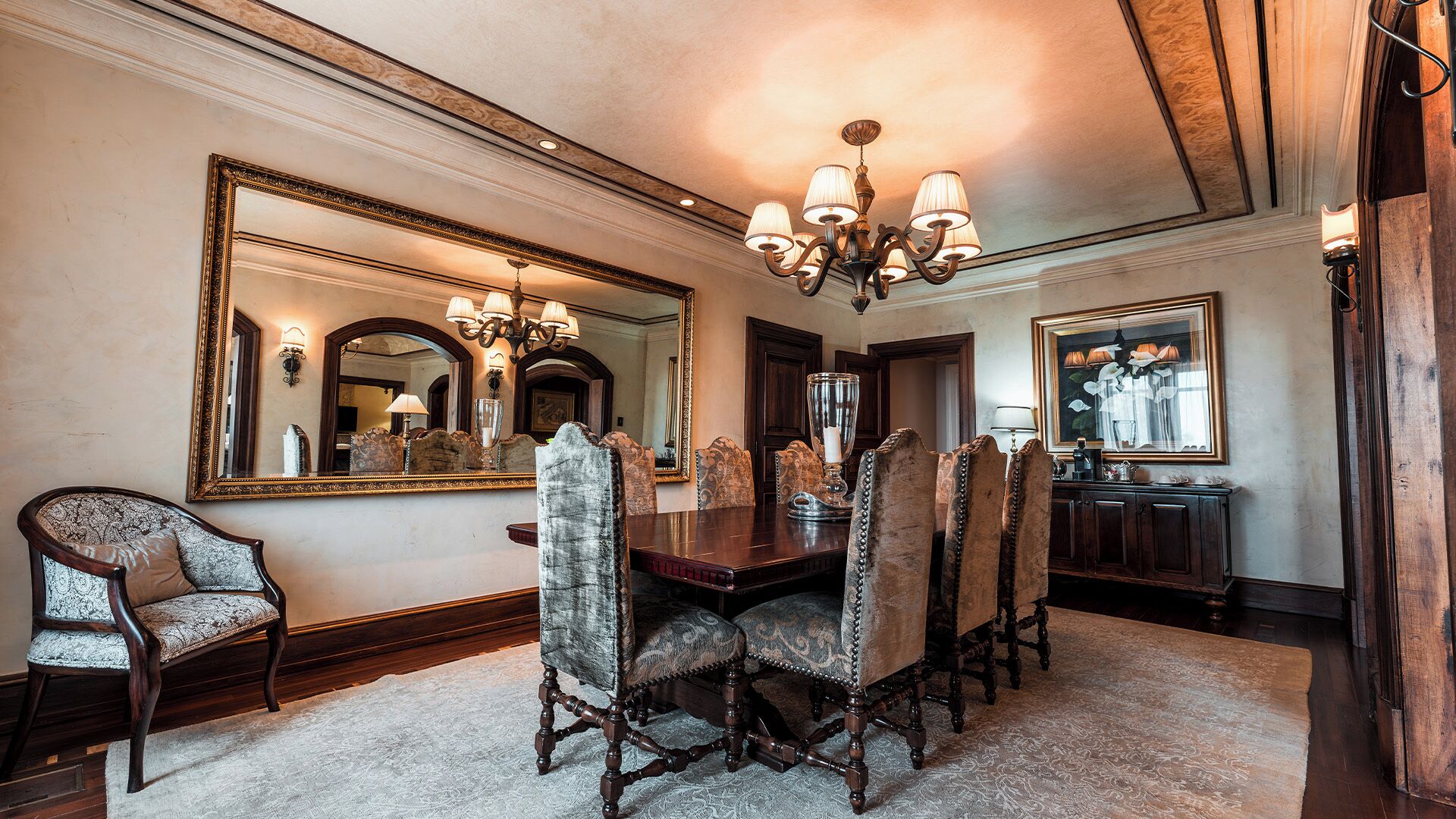 Uma sala de jantar formal com um espelho grande, lustre e móveis clássicos.