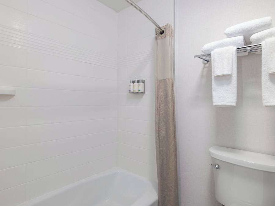 Um banheiro com paredes revestidas de azulejos brancos, uma banheira, um chuveiro cortinado e um vaso sanitário.