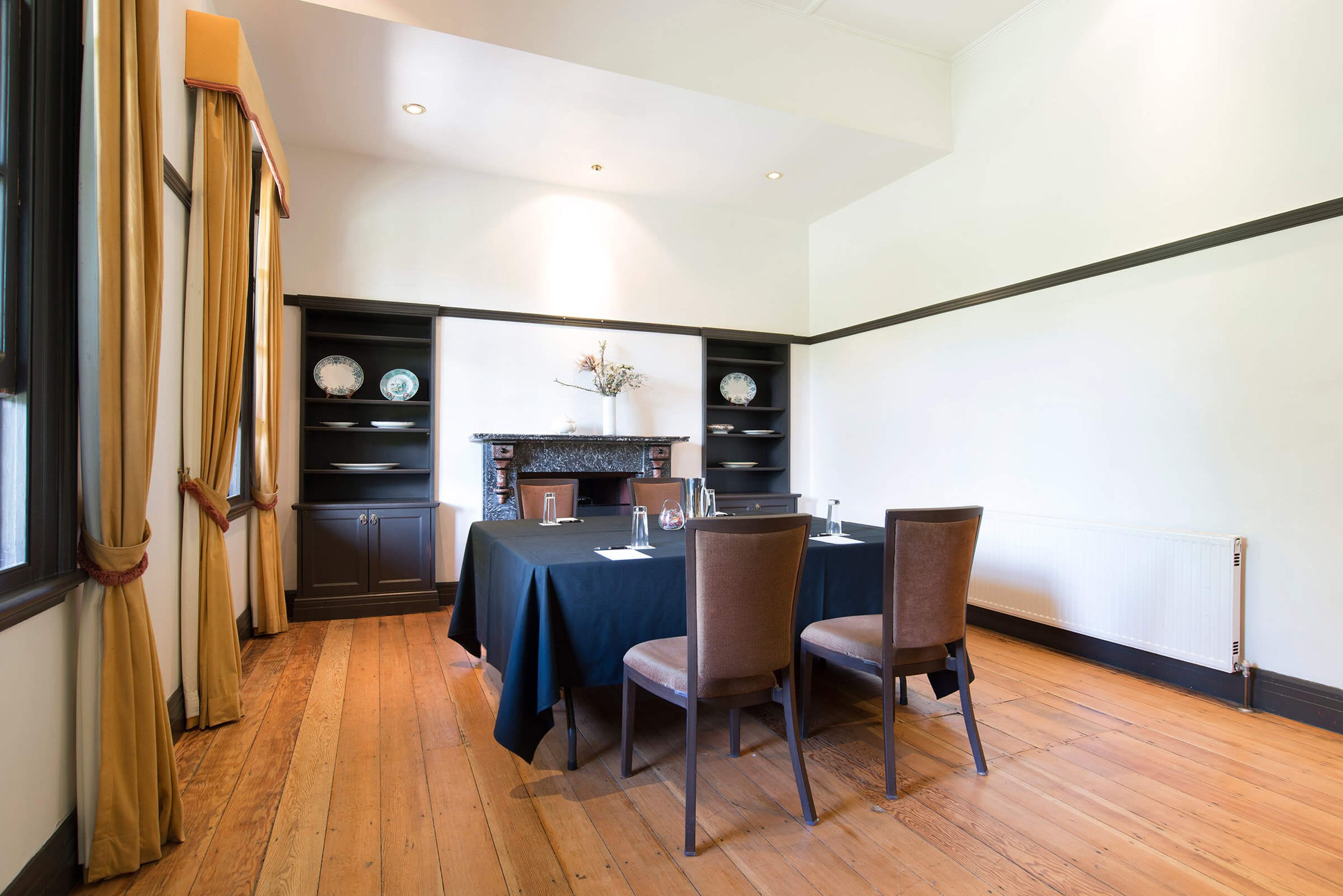 Uma sala de jantar com uma mesa posta para quatro pessoas, piso de madeira e esquema de cores preto e branco.