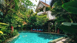 Piscina rodeada por vegetação exuberante, com espreguiçadeiras e área coberta.