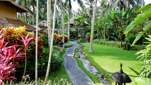 Um jardim tropical com um caminho de pedra, palmeiras e estruturas com telhados de palha.