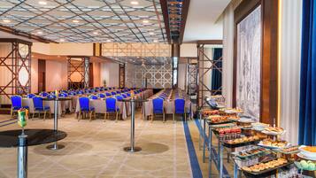Uma sala de banquetes com mesas compridas, cadeiras azuis e diversas mesas de comida.