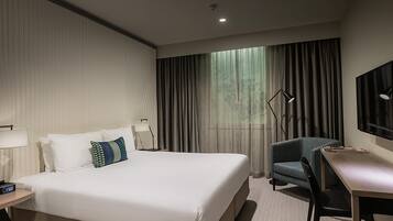 Quarto de hotel com uma cama grande, escrivaninha, cadeira, televisão e janela com cortinas.