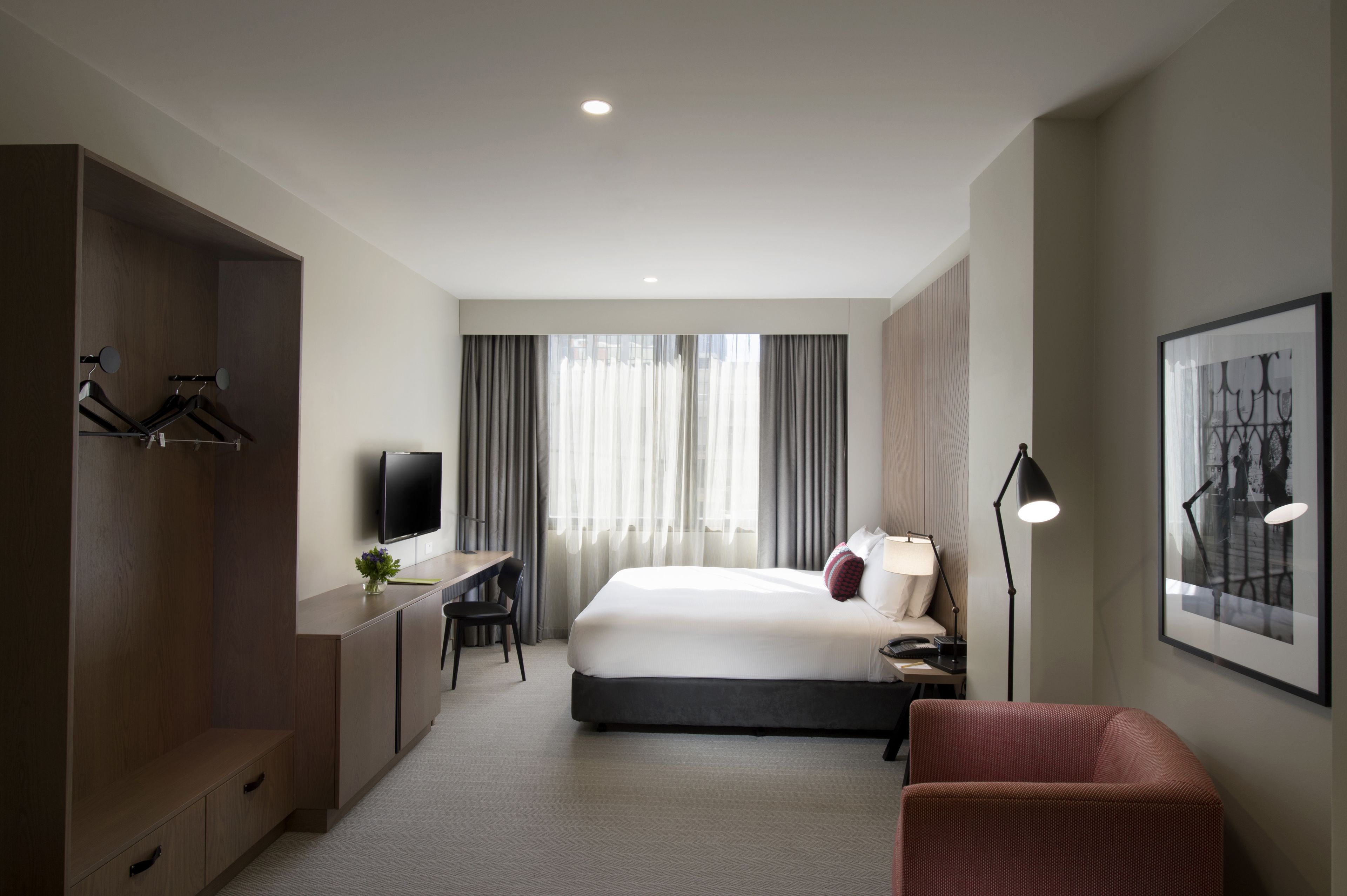Quarto de hotel com cama, escrivaninha, cadeira e televisão.