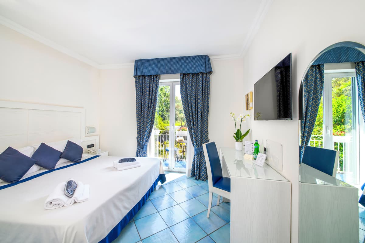 Quarto de hotel com cama, escrivaninha, cadeira, televisão e vista para o exterior.