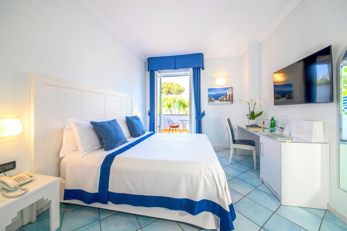 Quarto de hotel com cama, escrivaninha, cadeira, telefone e televisão.