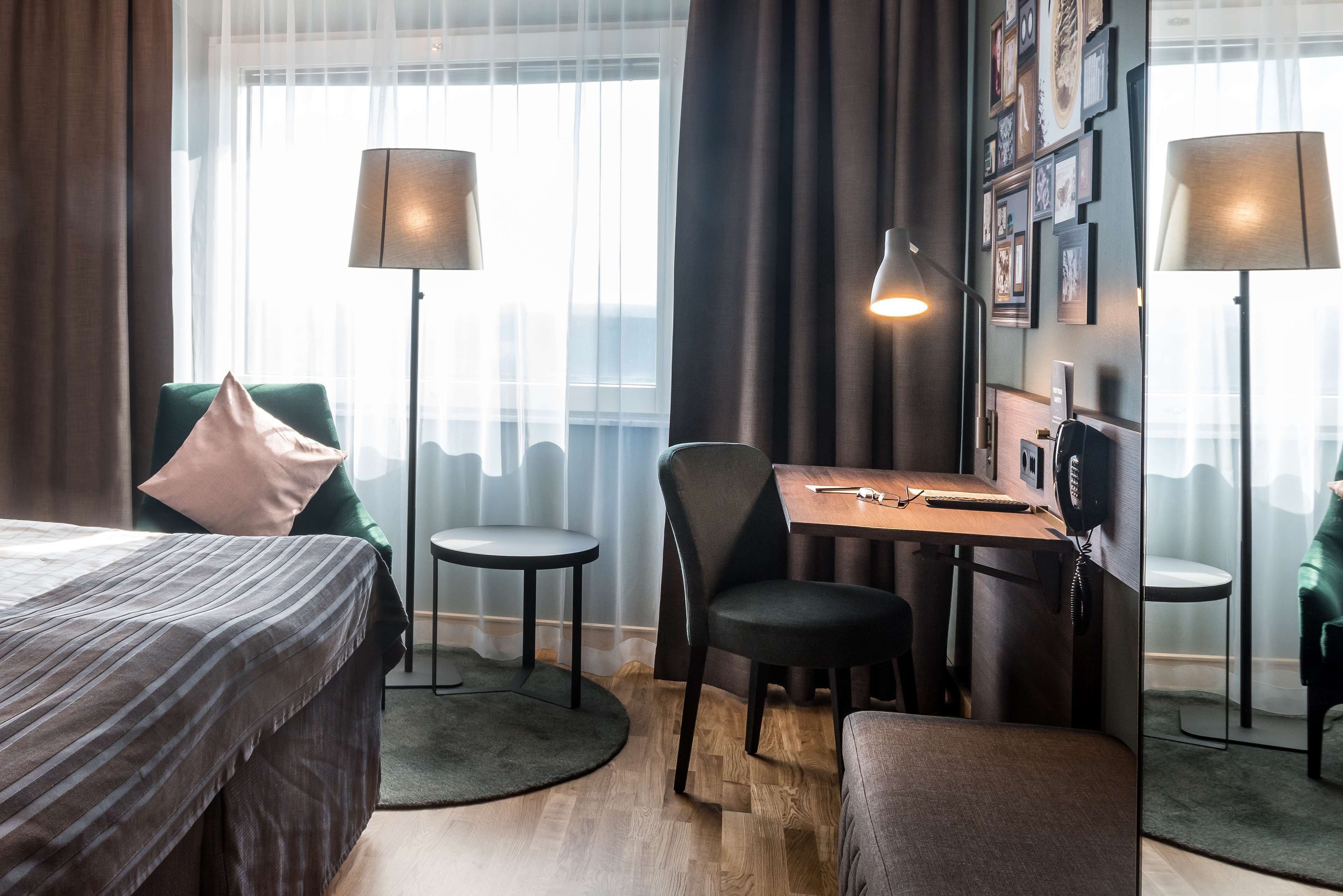 Quarto de hotel com cama, escrivaninha, cadeira, mesinha e abajur.