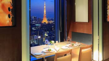 Uma área de refeições com vista para a Torre Eiffel à noite, com uma mesa posta para dois e cadeiras.