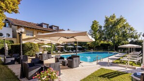 Uma área junto à piscina com espreguiçadeiras, guarda-sóis e uma piscina.