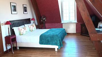 Quarto com teto de madeira, cama com colcha verde-água, um lustre e duas mesinhas com maçãs.