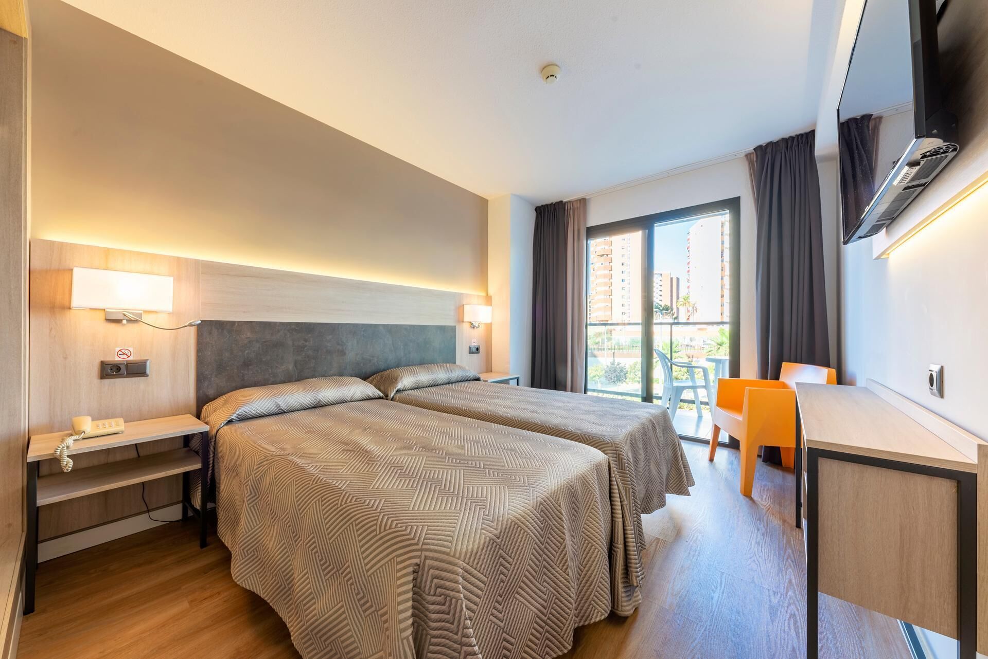 Quarto de hotel com duas camas, uma escrivaninha e varanda com vista.