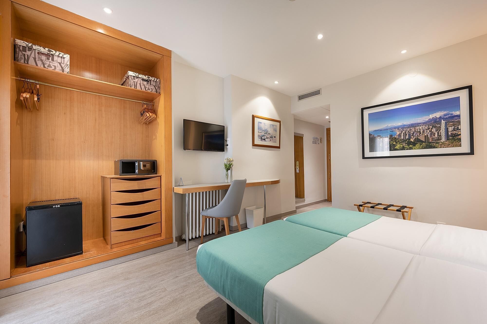 Quarto de hotel com cama, escrivaninha, televisão e vista para a paisagem urbana.