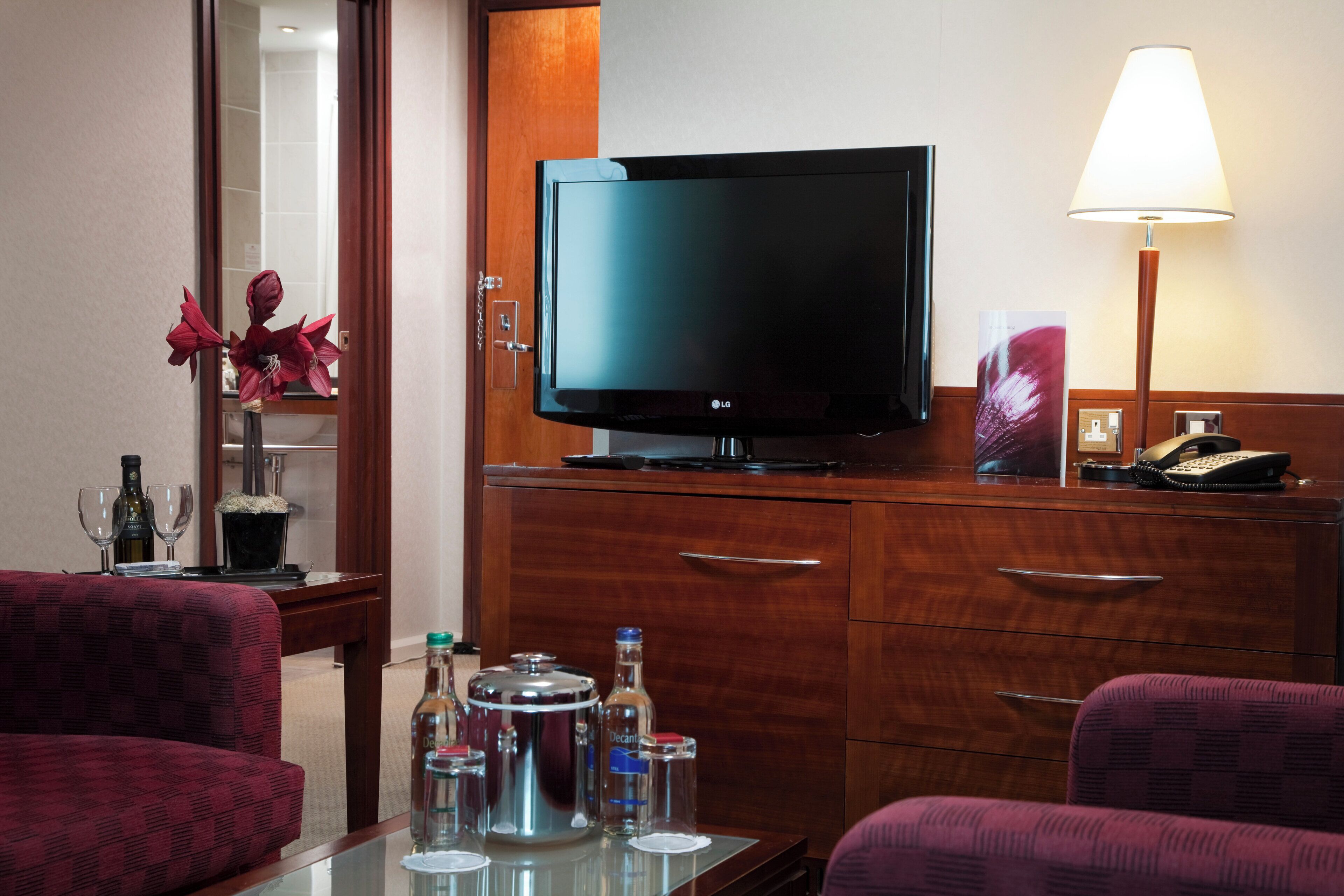 Quarto de hotel com televisão de tela plana, escrivaninha com abajur, telefone e minibar.