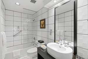 Um banheiro moderno com azulejos brancos, um espelho grande, uma banheira, um vaso sanitário e uma pia.