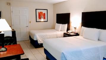 Quarto de hotel com duas camas, uma escrivaninha, uma cadeira, um quadro na parede e uma mesa de cabeceira com abajur.