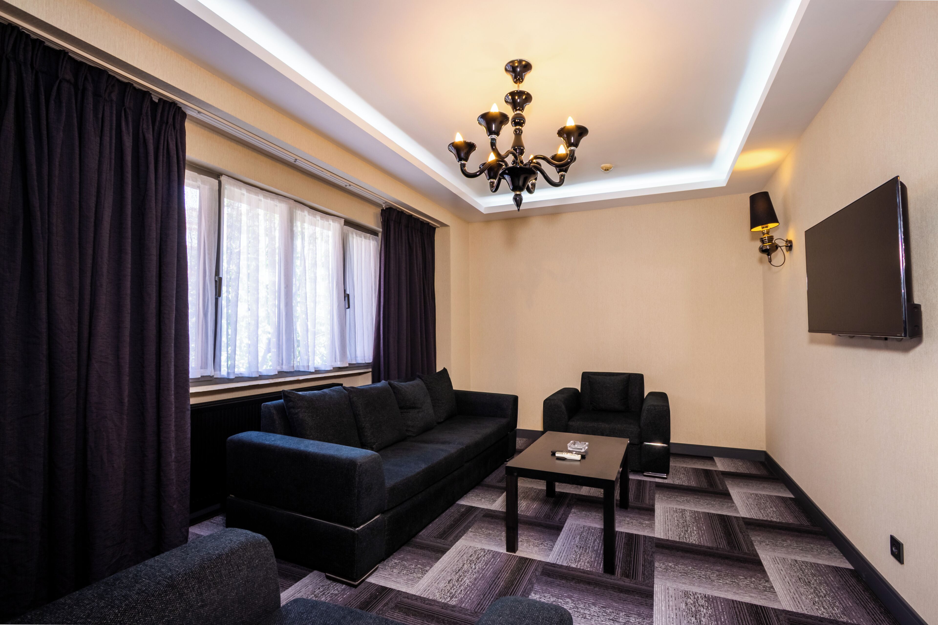 Uma sala de estar moderna com sofá, poltronas, mesa de centro, televisão e lustre.