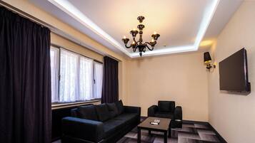 Uma sala de estar moderna com sofá, poltronas, mesa de centro, televisão e lustre.