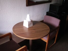 Uma mesa de madeira redonda com uma caixa de lenços, uma cadeira estofada roxa e outra de madeira.