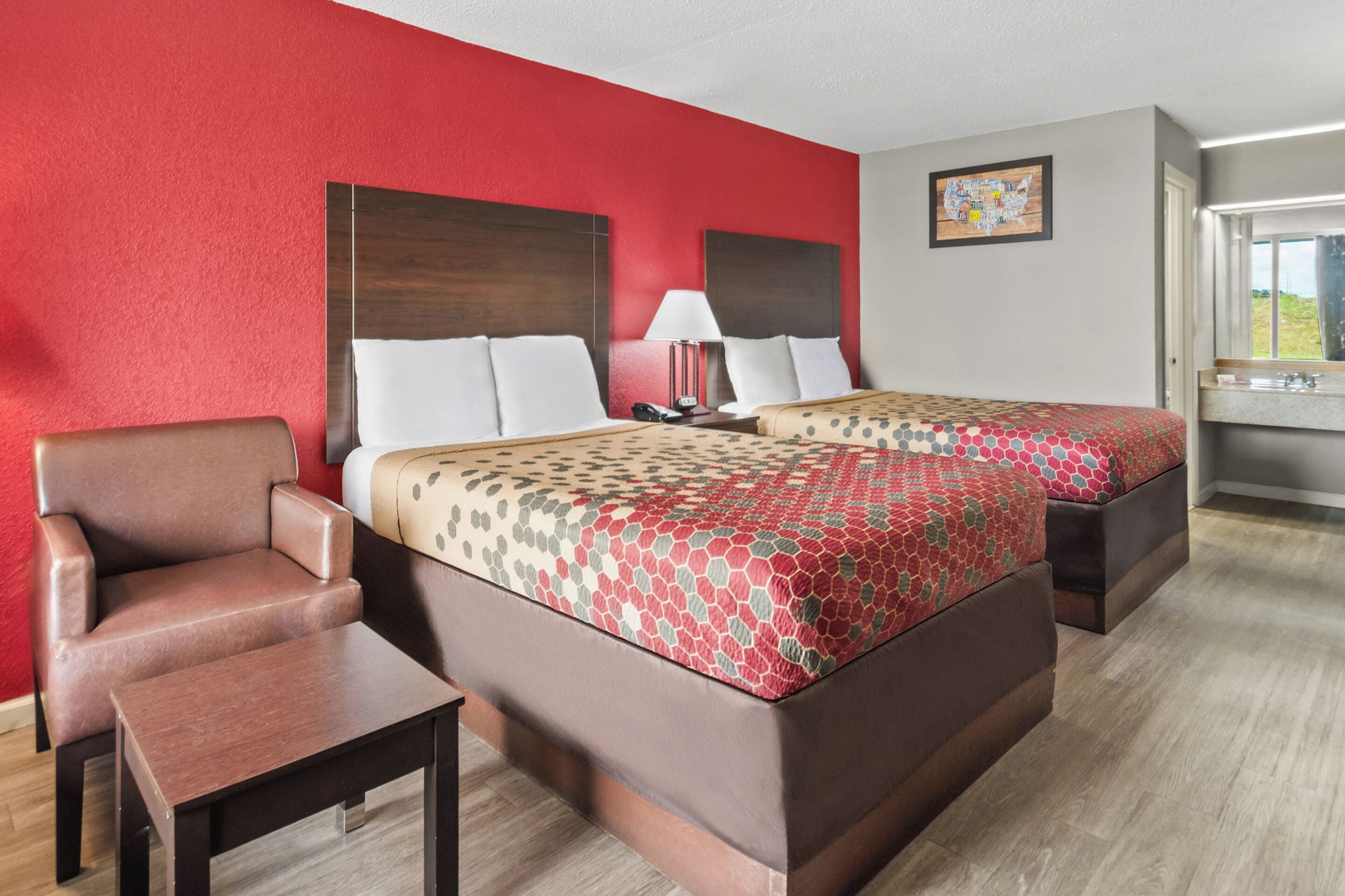 Quarto de hotel com duas camas, uma cadeira, uma mesinha de cabeceira e uma janela.