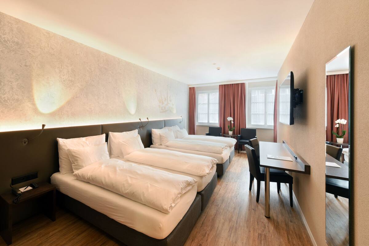Quarto de hotel com três camas, uma escrivaninha e uma cadeira.