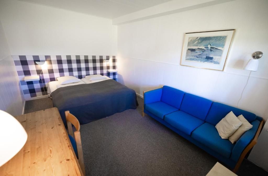 Quarto com cama, sofá azul, mesa de madeira e uma obra de arte na parede.