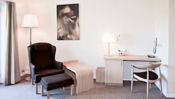 Quarto de hotel com uma secretária, duas cadeiras, uma lâmpada, um quadro na parede e uma janela com cortinas.