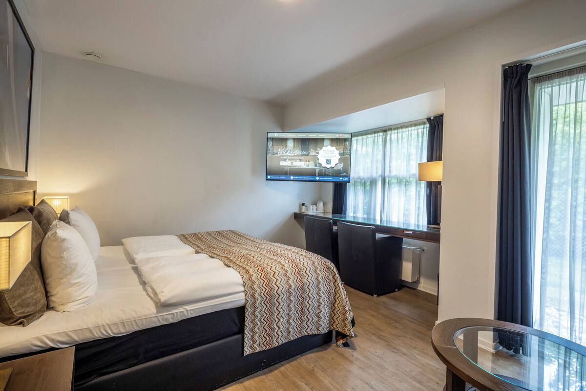 Quarto de hotel com cama, escrivaninha e televisão.